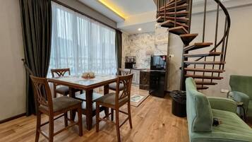 Uma sala de jantar com mesa e cadeiras, uma escada em espiral, um sofá verde e uma cozinha.