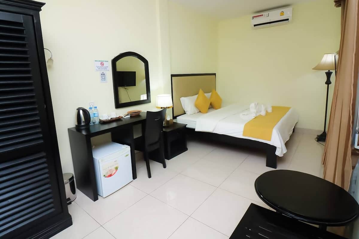 Quarto de hotel com cama, escrivaninha, cadeira e pequeno frigorífico.