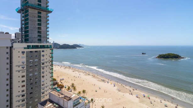 Uma praia com um edifício alto em primeiro plano e uma pequena ilha ao longe.