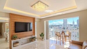 Sala de estar moderna com televisão de tela plana, varanda com conjunto de jantar e vista para a cidade.