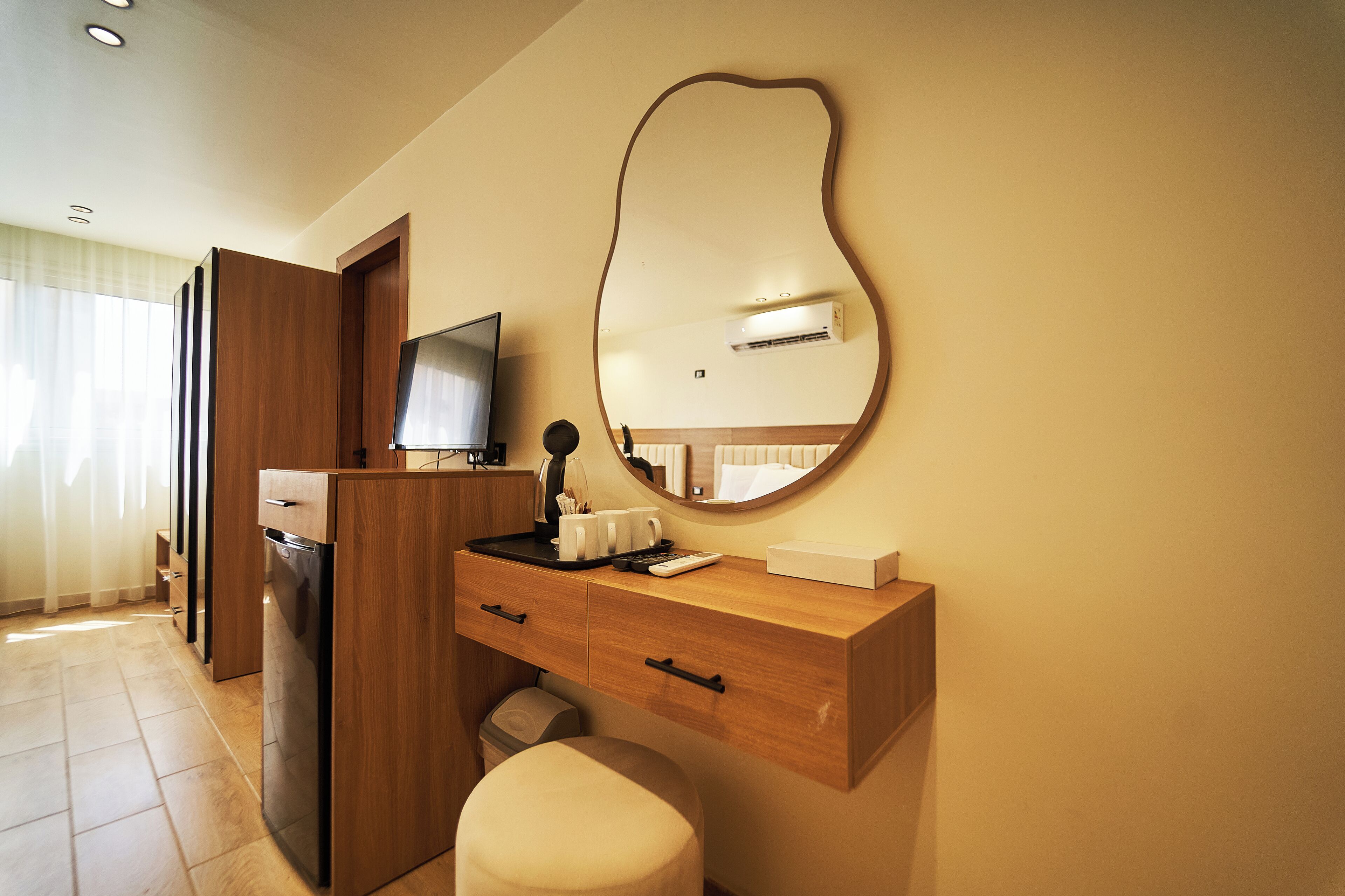Quarto de hotel com uma toucador de madeira, um espelho, uma televisão e um pequeno banquinho.