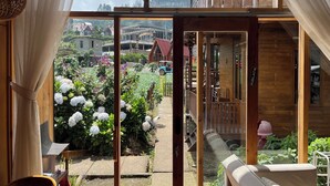 Vista de um quarto com uma janela grande, mostrando um jardim com hortênsias e um carro azul estacionado na frente.