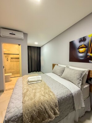 Quarto de hotel moderno com uma cama grande, área de chuveiro e um quadro na parede.