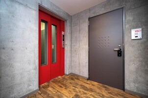 Corredor com uma porta vermelha e uma porta cinza, ambas equipadas com sistemas de segurança modernos.