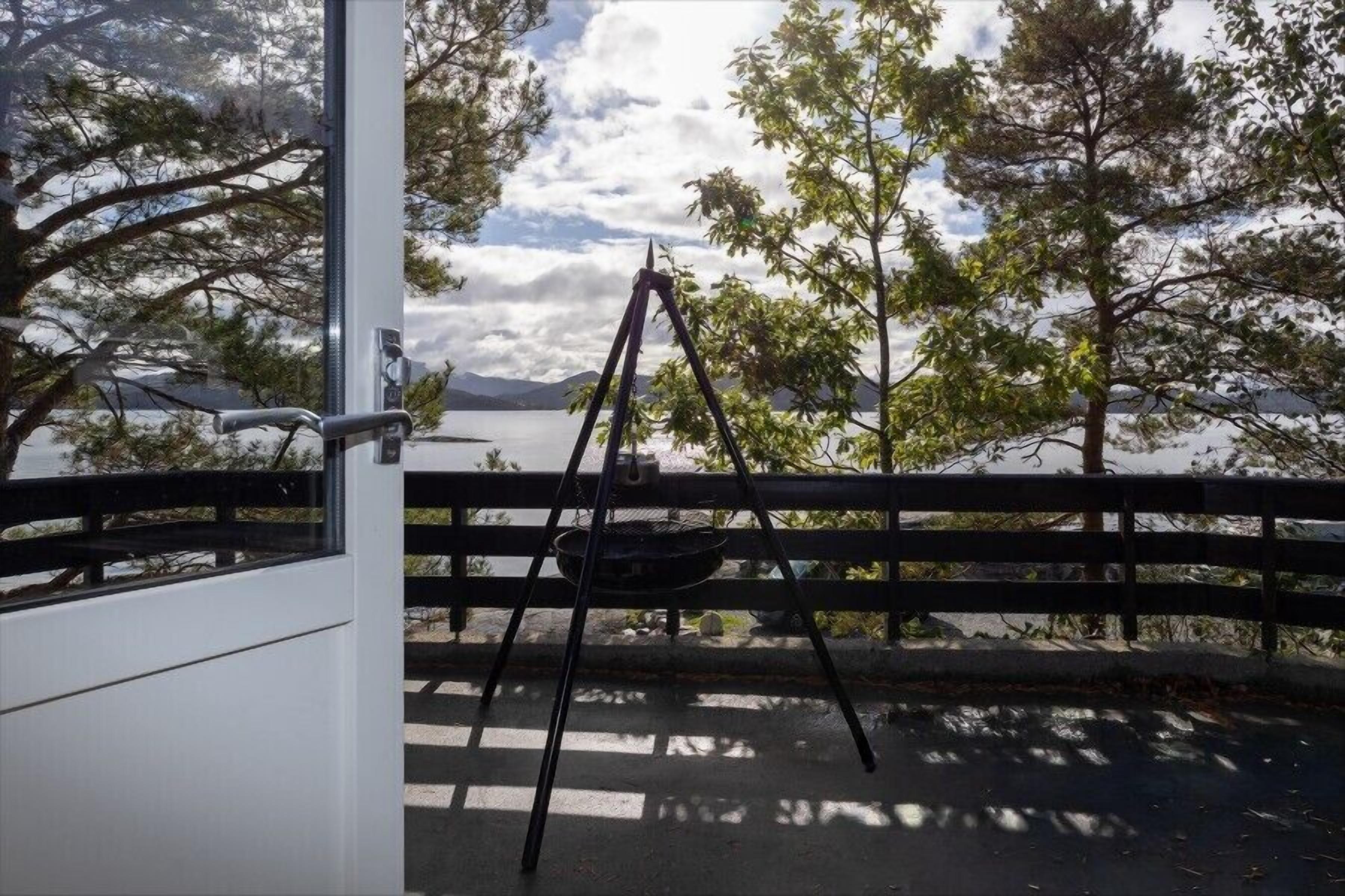 Um banco com um tripé e uma panela, com vista para um lago, árvores e montanhas ao fundo.