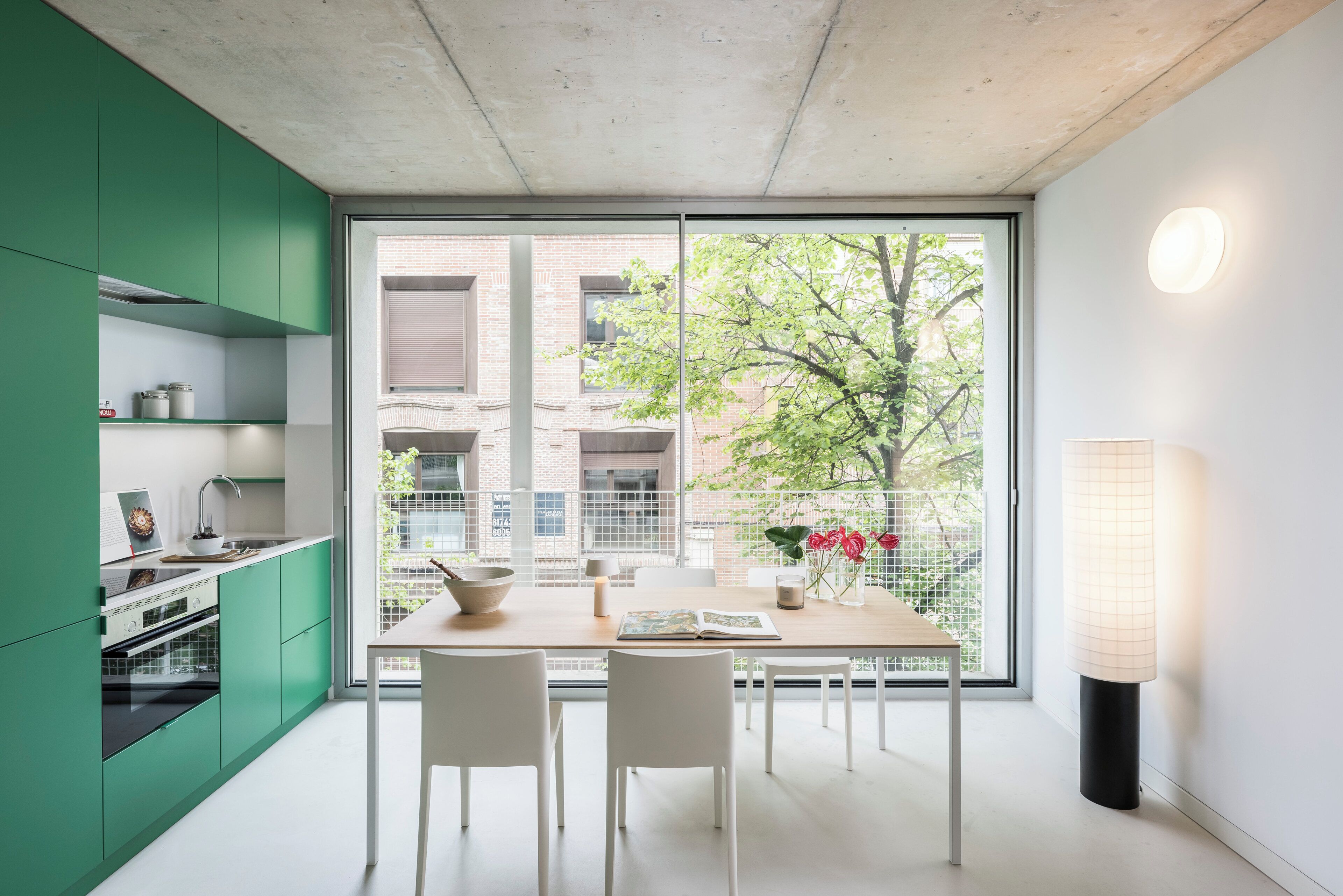 Uma cozinha moderna com armários verdes, uma janela grande e uma mesa com cadeiras.