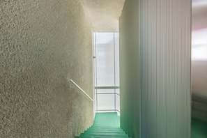Uma escadaria com uma parede texturizada de um lado e outra lisa, conduzindo a um espaço interior iluminado.