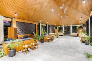 Amplo espaço interno com teto de madeira, balcão de recepção, áreas de estar e plantas em vasos.