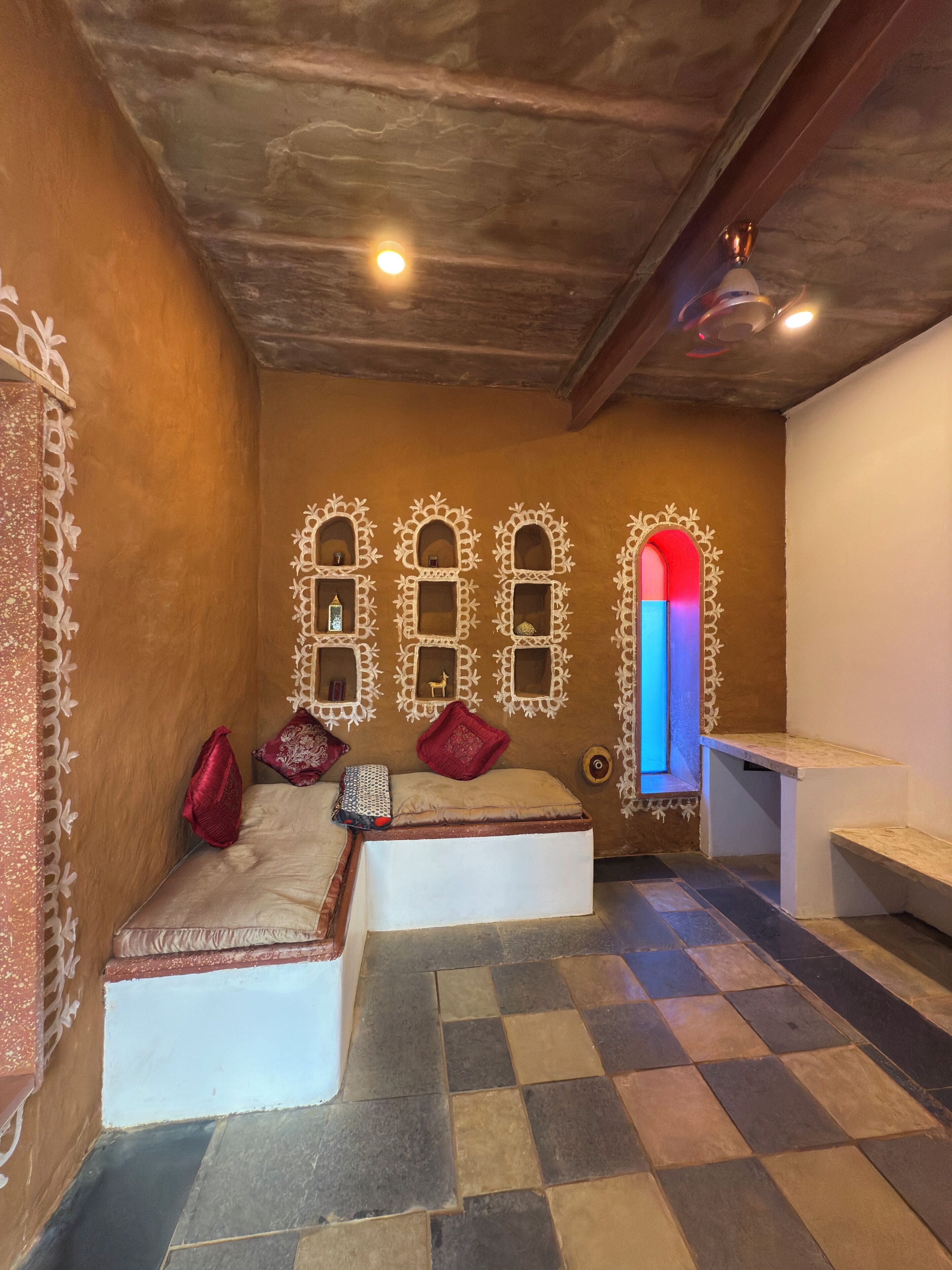 Um quarto com piso xadrez, um banco com almofadas e uma parede com arcos decorativos.