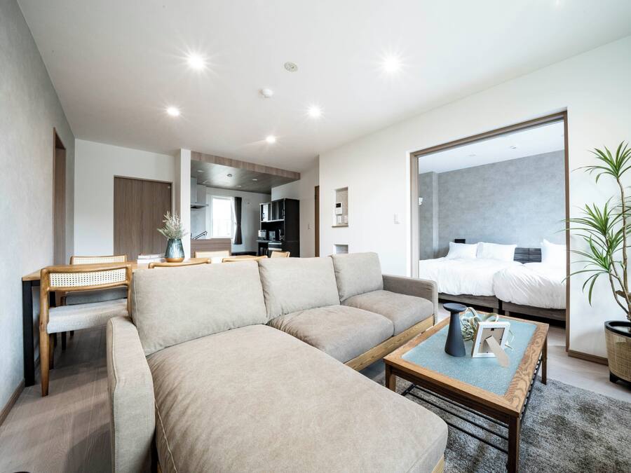 Sala de estar moderna com sofá, mesa de centro e área de jantar. Uma cama ao fundo com vista para a cidade.