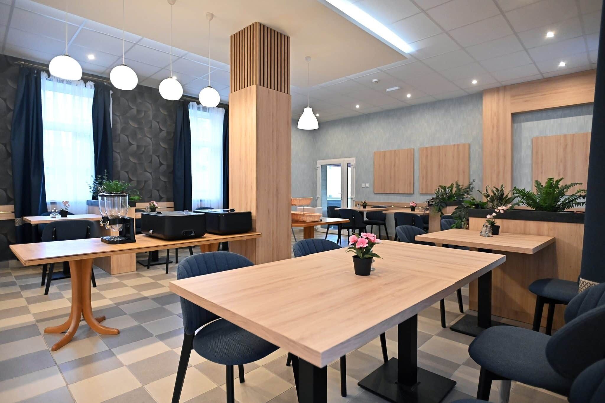 Um café moderno com mesas de madeira, cadeiras pretas e iluminação pendente.