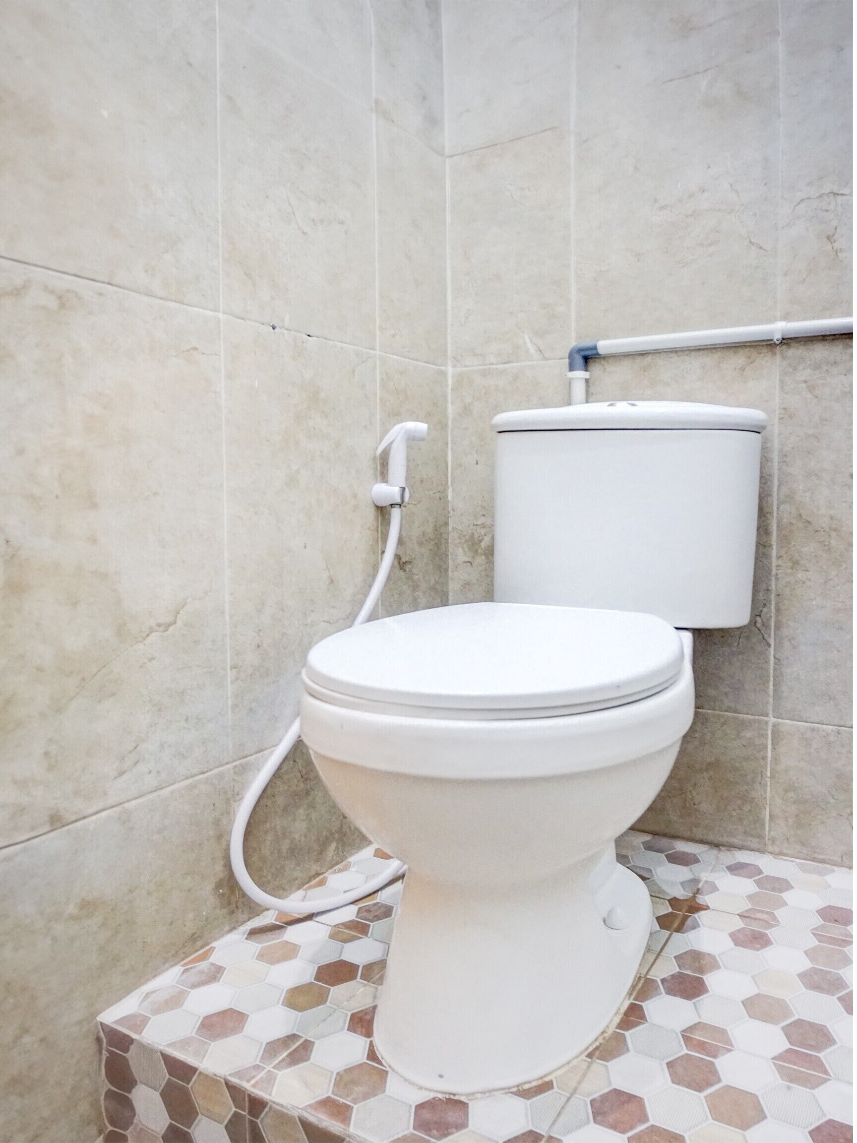 Sanitário com caixa de água e tampa brancos, acionador de descarga branco e cano branco.