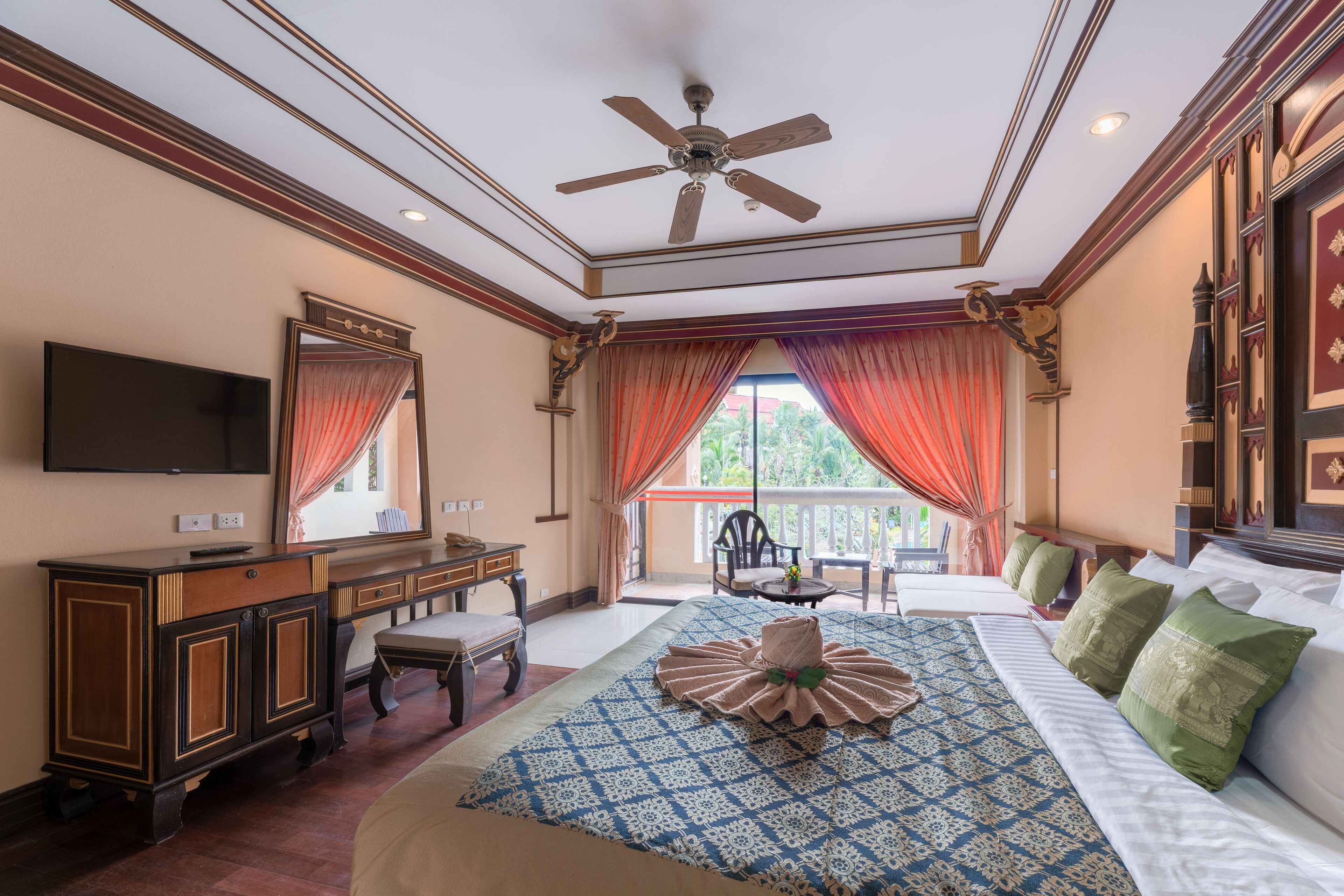Quarto de hotel com cama, escrivaninha, cadeira, televisão e varanda com cortinas vermelhas.