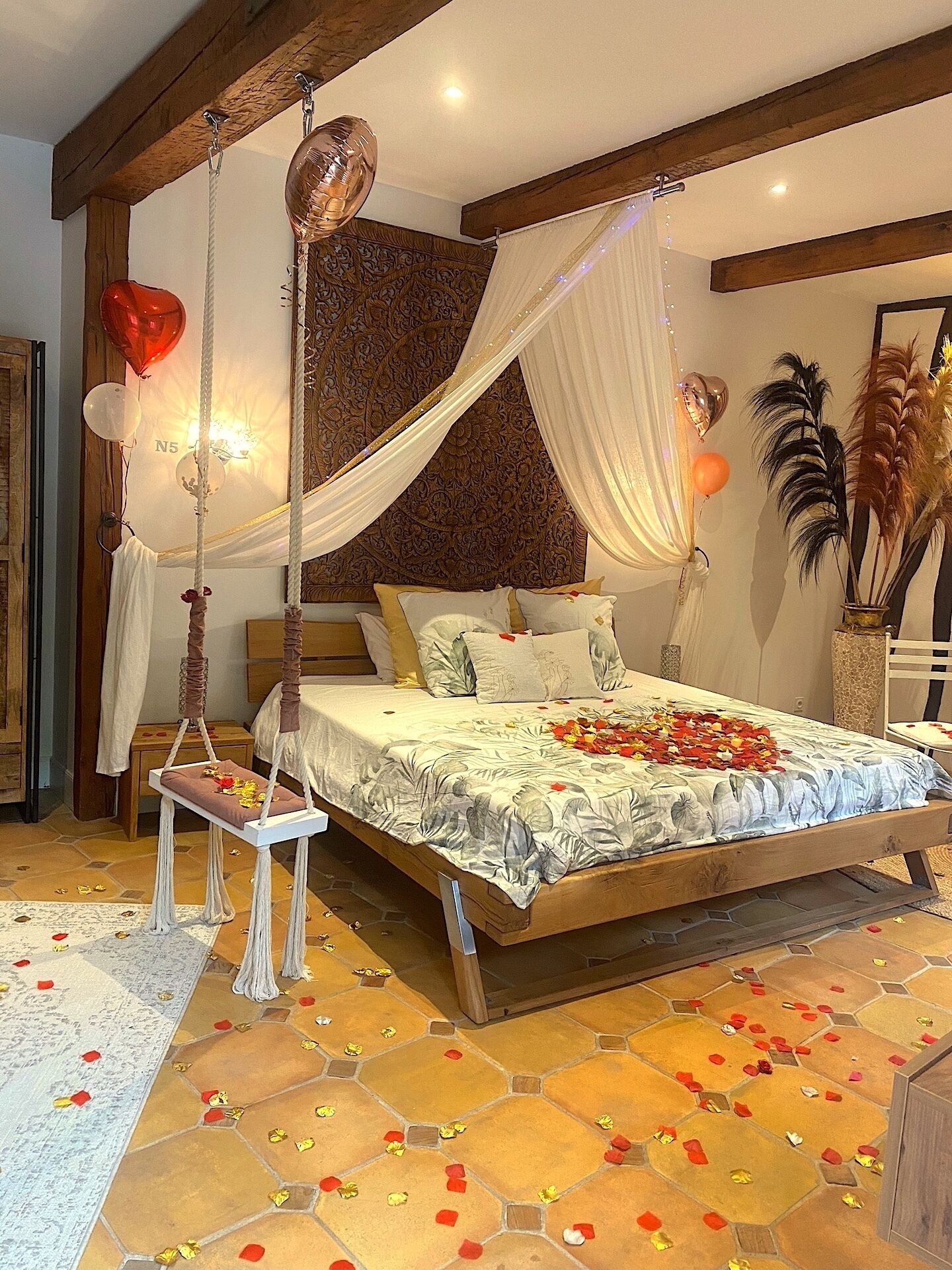 Quarto com cama, cadeira suspensa, lustre e detalhe decorativo na parede.