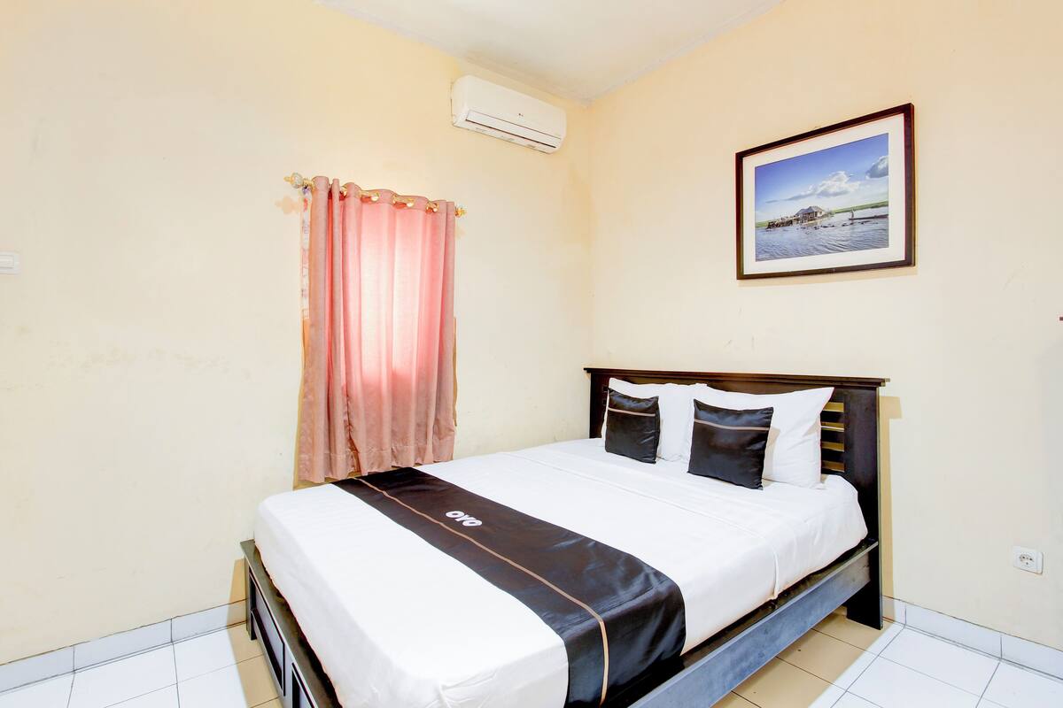 Cama bem arrumada com colcha preta e branca, um único travesseiro e um cobre-leito decorativo.
