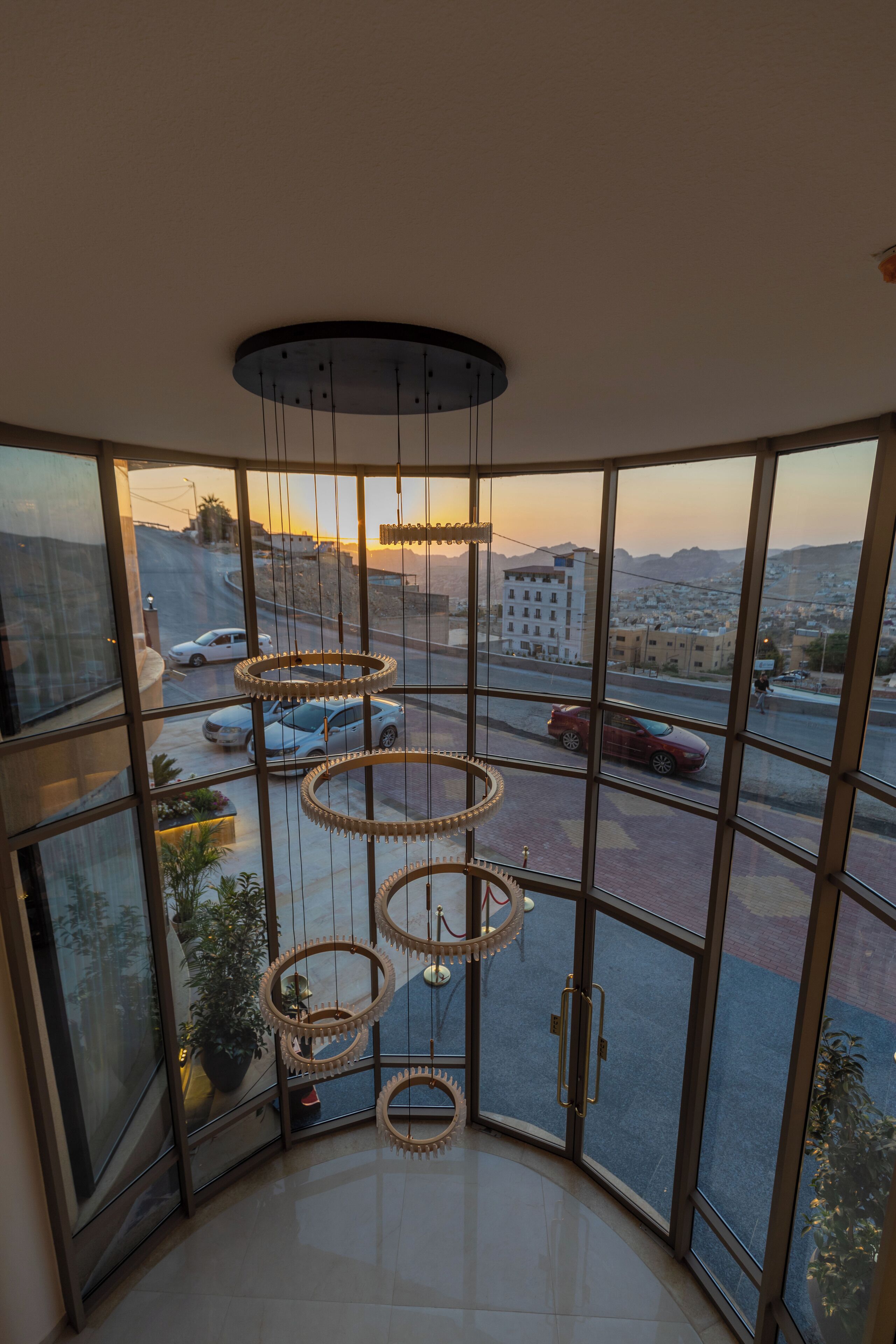 Quarto de canto com grandes janelas, luminária circular e vista para a paisagem urbana.