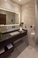 Um banheiro moderno com toucador de mármore, um espelho grande com iluminação embutida, chuveiro manual e porta-toalhas.