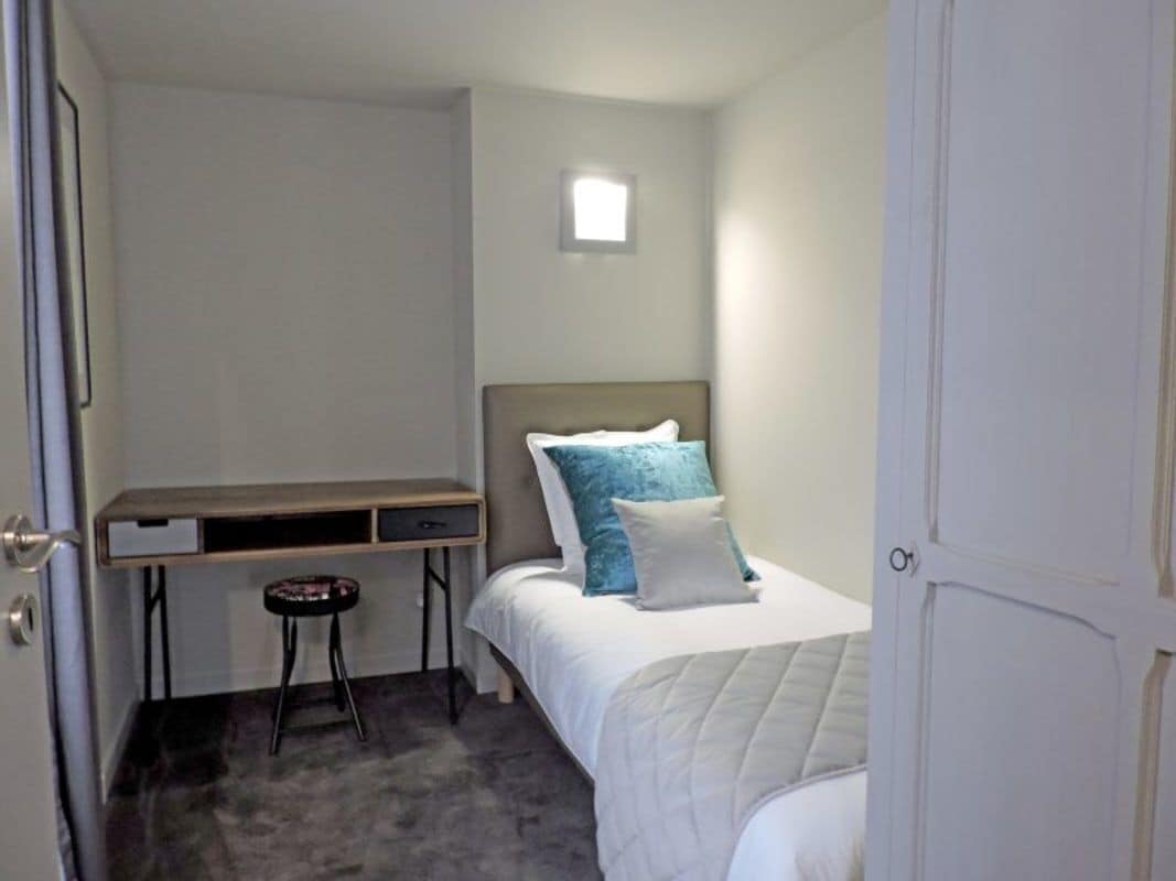 Quarto com uma cama, uma escrivaninha e um banquinho.