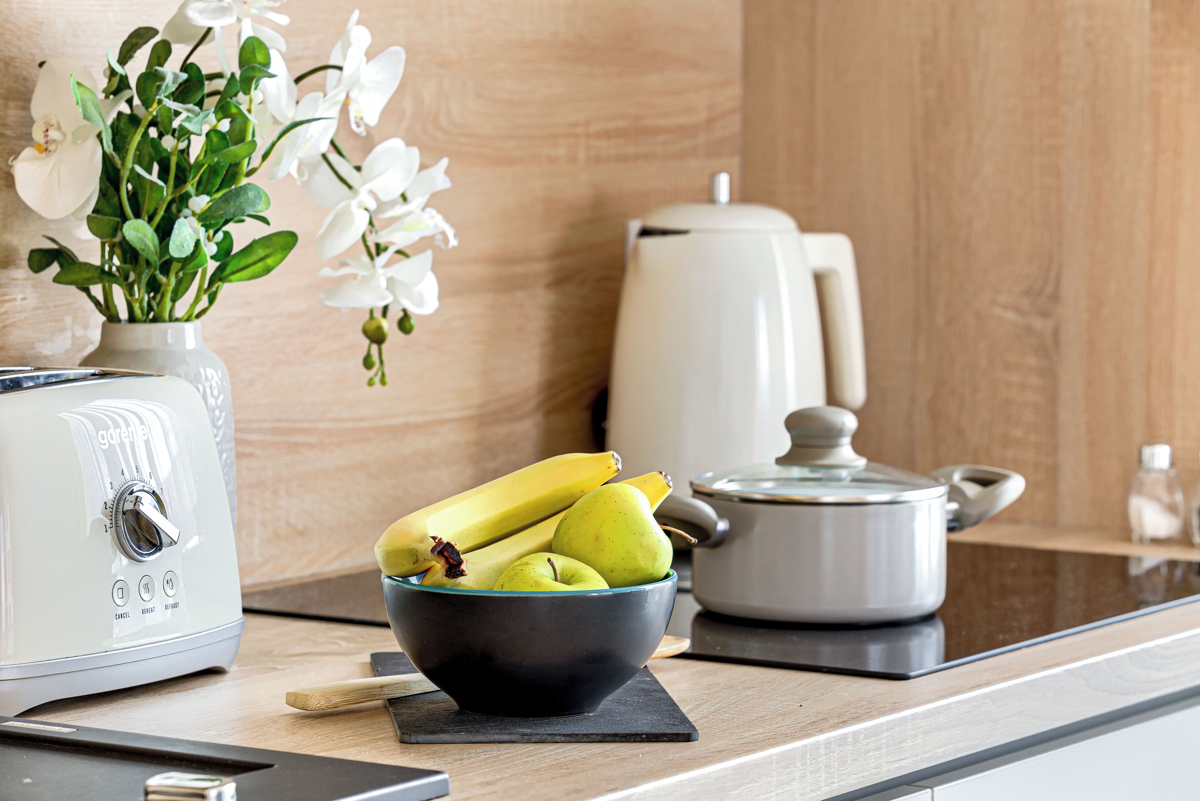 Uma bancada de cozinha com uma tigela de frutas, um eletrodoméstico branco e uma panela branca.