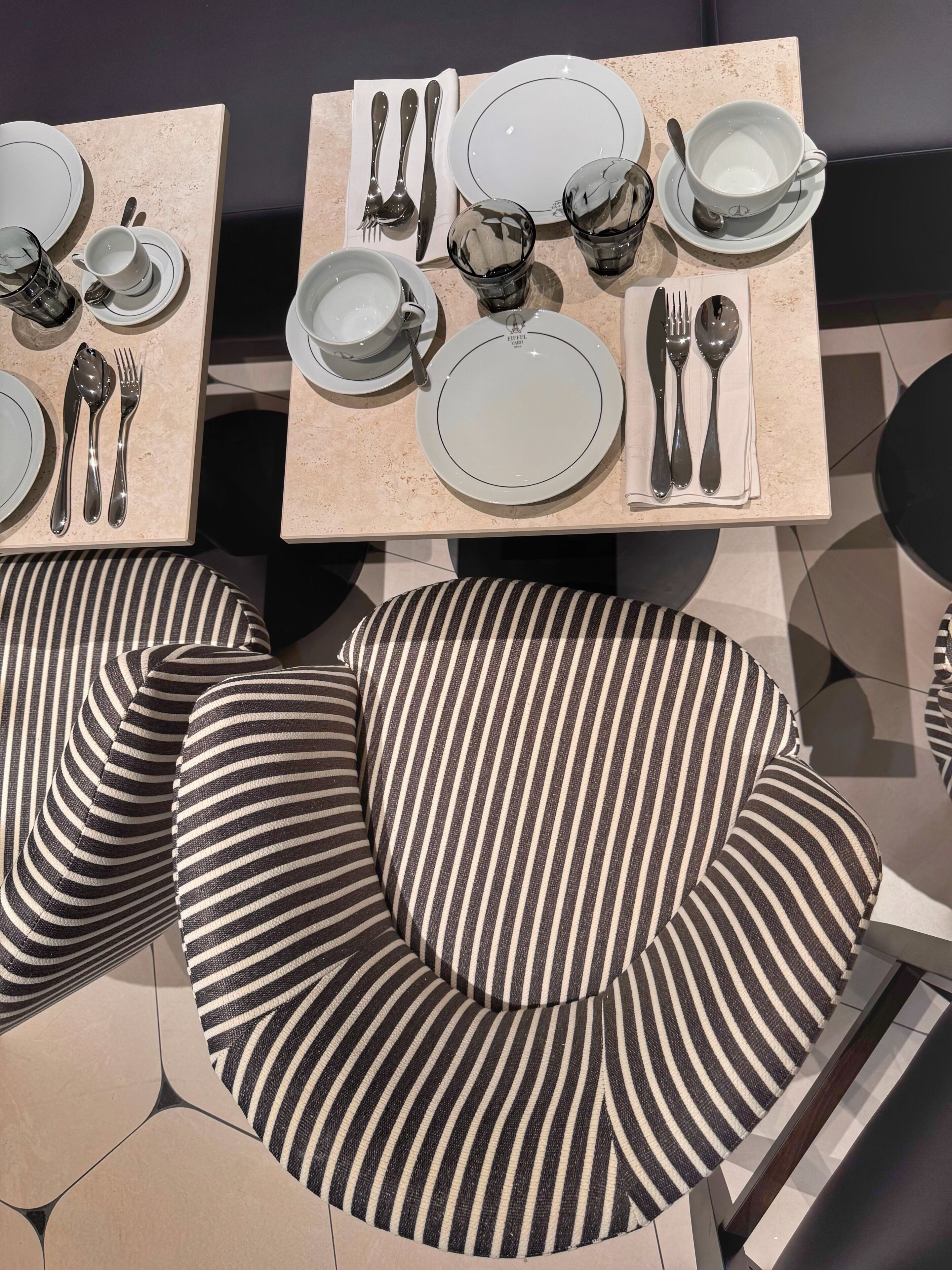 Uma sala de jantar com assentos acolchoados listrados, uma mesa posta com pratos, talheres e copos.