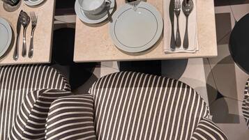 Uma sala de jantar com assentos acolchoados listrados, uma mesa posta com pratos, talheres e copos.