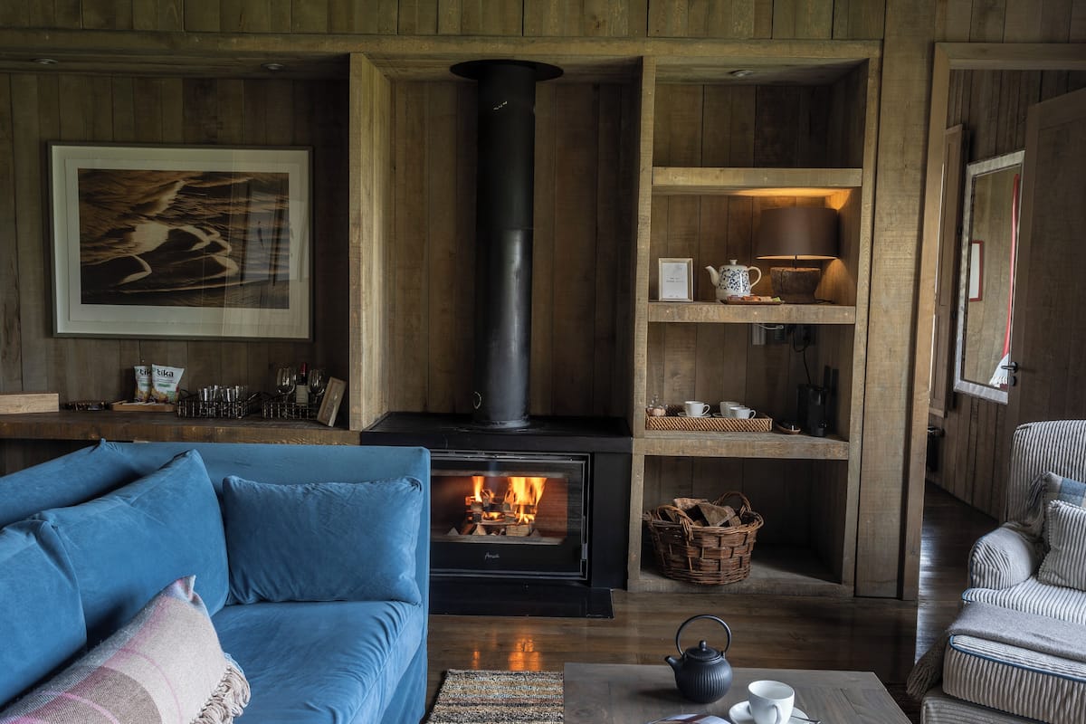Uma sala de estar aconchegante com um sofá azul, uma lareira, estantes com objetos decorativos e uma obra de arte emoldurada na parede.