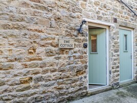 Um edifício de pedra com uma placa que diz 'EWE COTTAGE' e duas portas.