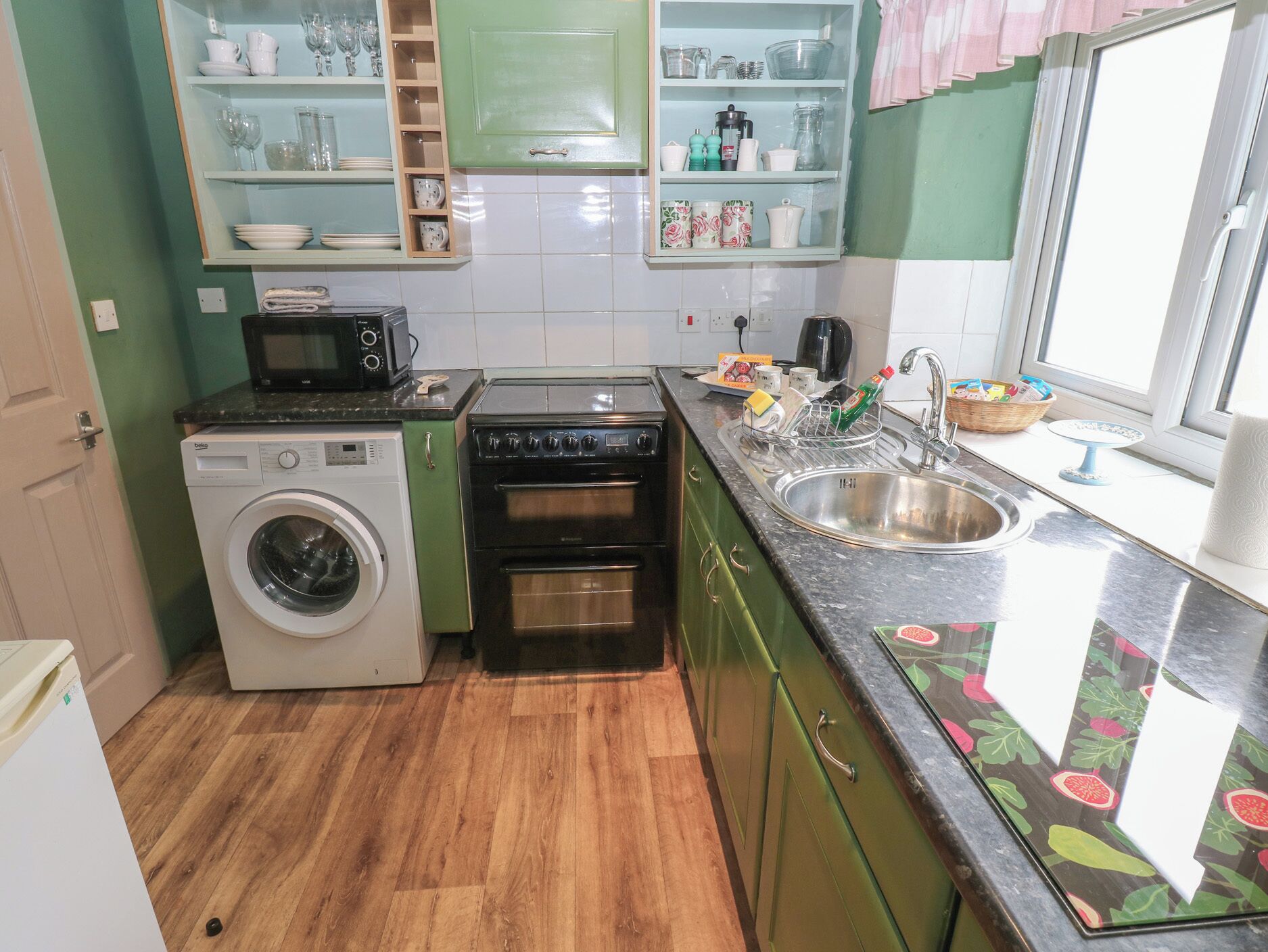Uma cozinha compacta com máquina de lavar, micro-ondas, forno e pia com janela acima.