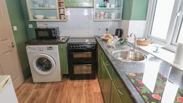 Uma cozinha compacta com máquina de lavar, micro-ondas, forno e pia com janela acima.