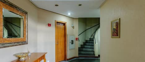 Um corredor com um aparador de madeira, um espelho, uma porta e uma escada.