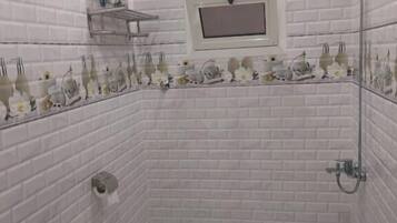 Casa de banho com azulejos brancos, sanita, chuveiro e uma pequena janela acima do espelho.