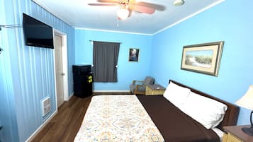 Quarto com cama, ventoinha no teto, televisão, micro-ondas, mesa pequena e uma cadeira.