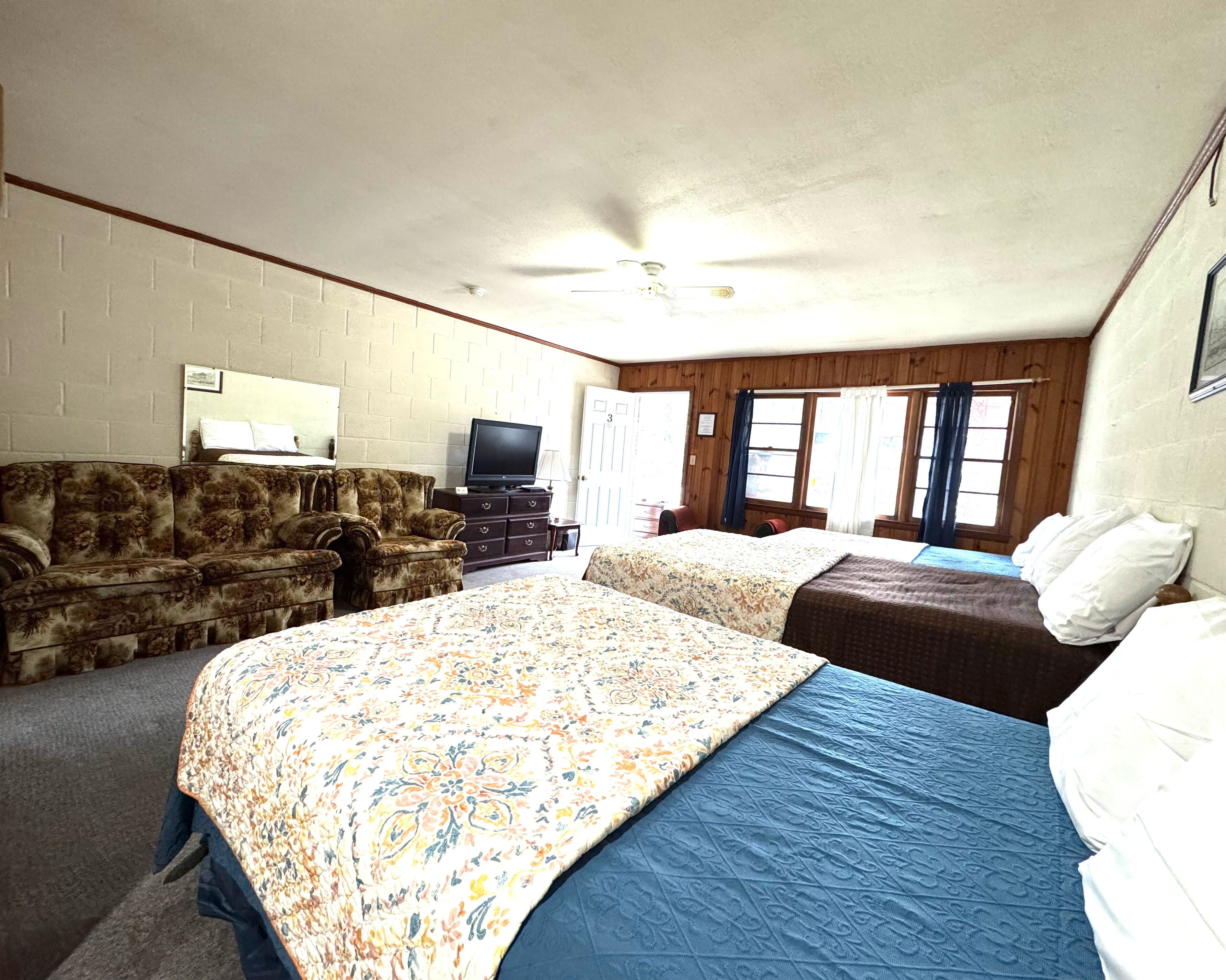 Quarto de motel com uma cama grande, um sofá, uma TV e uma janela com cortinas.