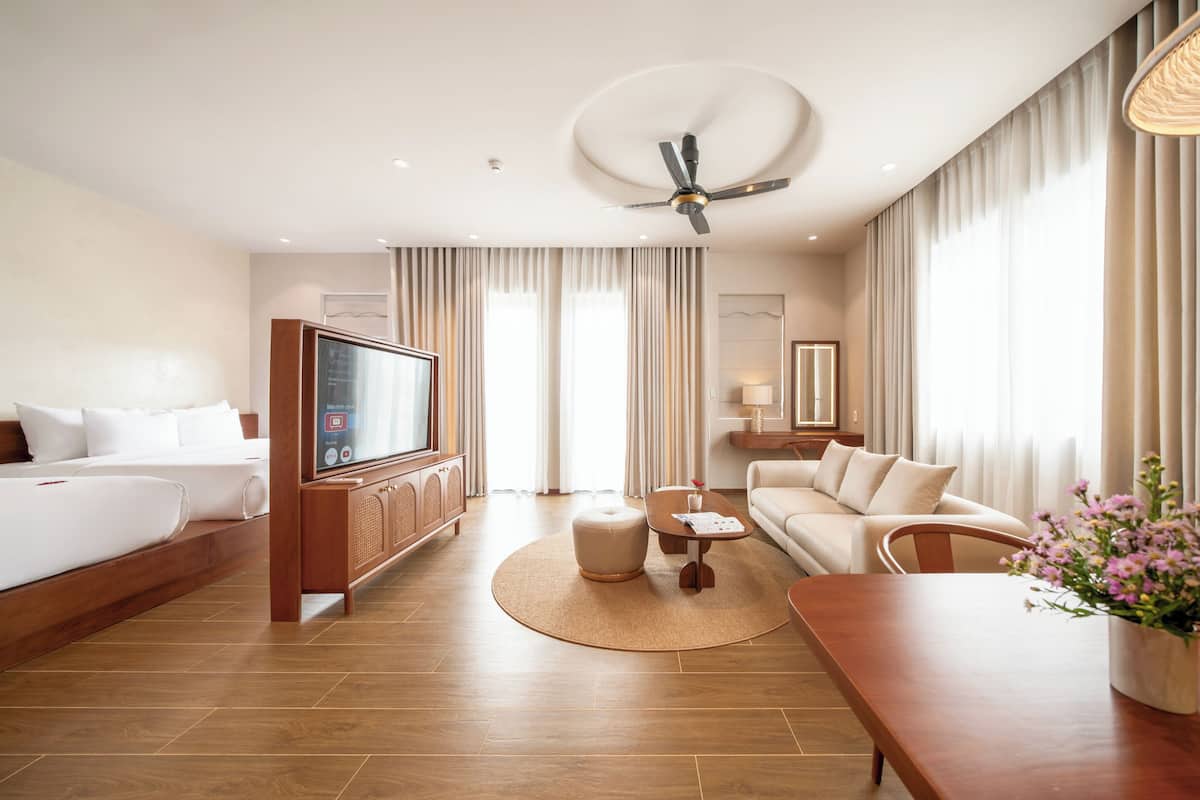 Quarto de hotel com uma cama, televisão, sofá, mesa de centro e mesa de jantar.