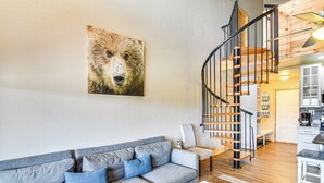 Uma sala de estar moderna com um sofá cinzento, uma mesa de centro de madeira e um quadro de um urso na parede.