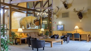 Um hall espaçoso com uma grande mesa de madeira, poltronas de couro e um urso polar montado na parede.