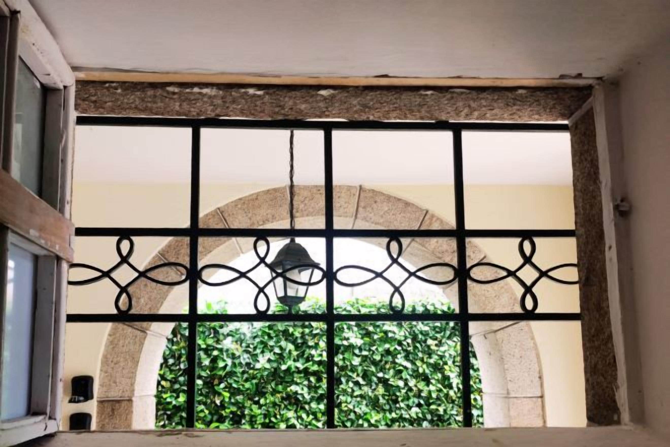 Visão através de uma janela com grades, uma estrutura de pedra em arco e um candeeiro suspenso.