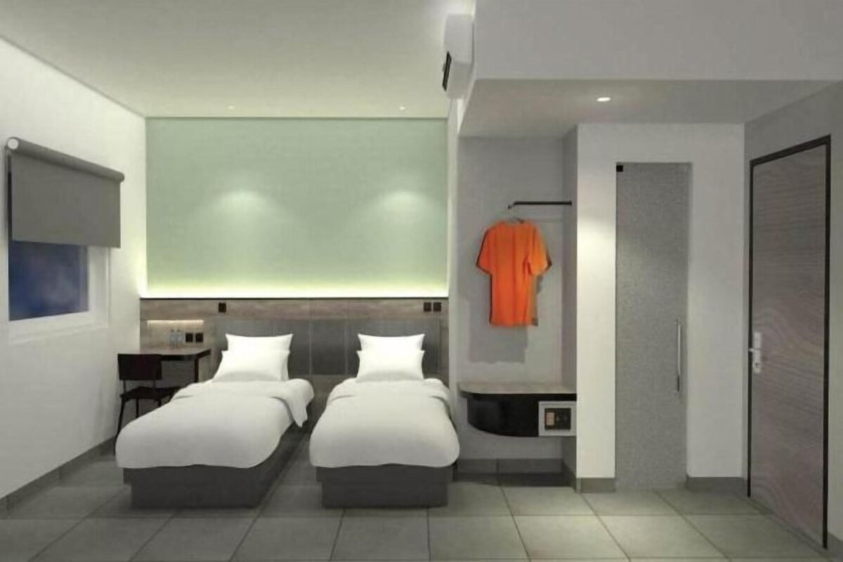 Quarto de hotel moderno com duas camas, uma pequena escrivaninha, um guarda-roupa e uma janela grande.