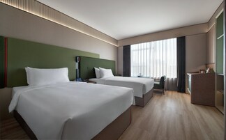 Quarto de hotel com duas camas, uma escrivaninha, uma cadeira e uma janela com cortinas.