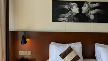 Quarto de hotel com uma cama, um quadro, ar condicionado, abajur e telefone sobre uma mesa pequena.