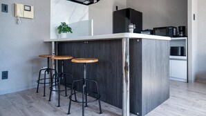 Uma cozinha moderna com uma ilha central, três banquetas, fogão embutido e micro-ondas.