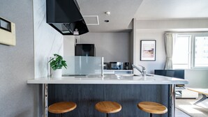 Uma cozinha moderna com bancada branca, três banquetas de madeira, exaustor preto e um vaso com planta.