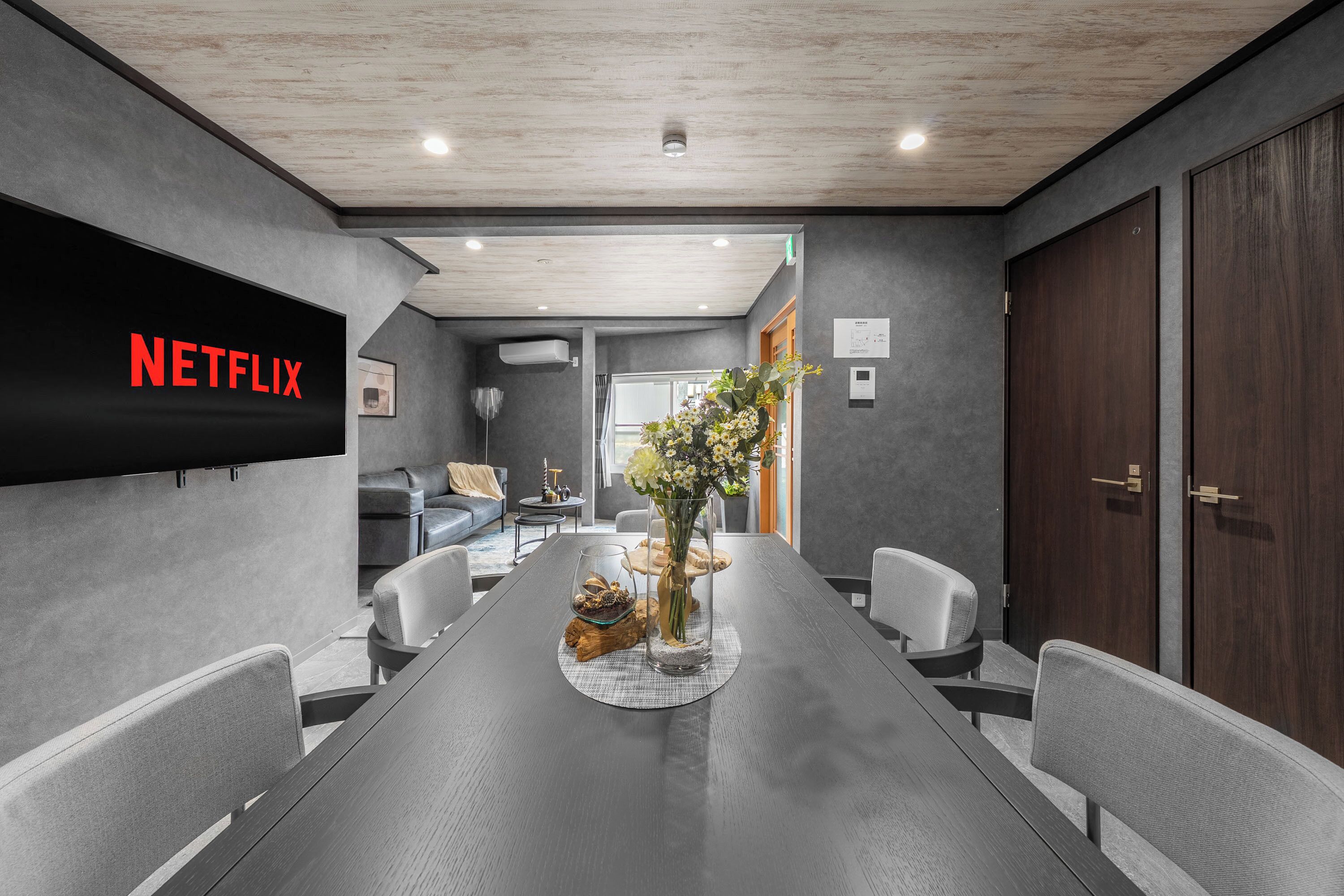 Uma sala de conferências com uma mesa comprida, cadeiras, um vaso com flores e uma TV fixada na parede exibindo o logotipo da Netflix.
