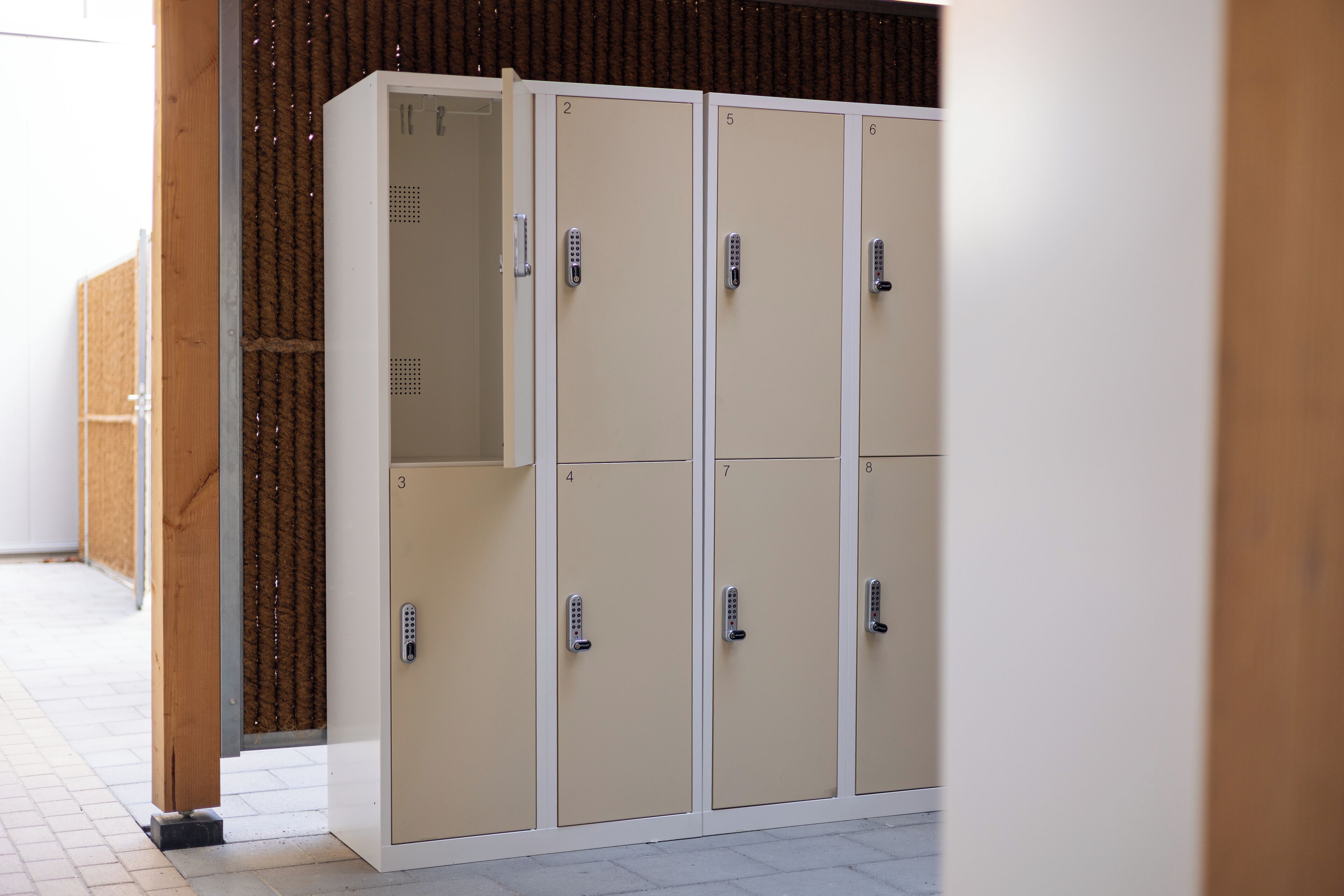 Uma fileira de armários bege com portas numeradas, cada um com fechadura.