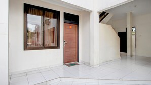 Uma entrada limpa e moderna, com uma porta castanha, uma janela com cortinas e chão em mosaico.