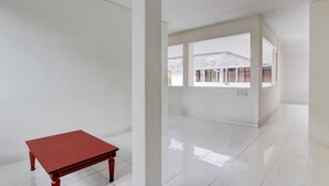 Um quarto espaçoso com uma mesa vermelha, paredes brancas e vista para um edifício pela janela.