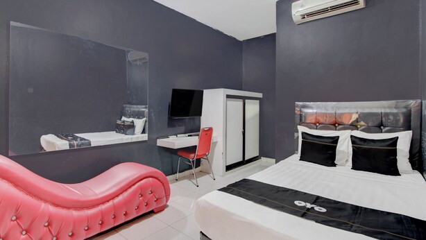 Quarto de hotel moderno com uma cama grande, um sofá rosa, uma escrivaninha com cadeira, um guarda-roupa e uma televisão.