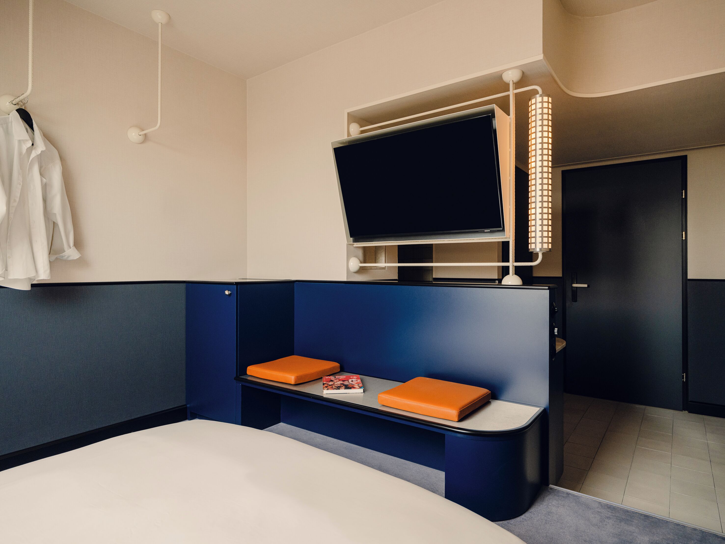 Quarto de hotel com cama, escrivaninha com televisão de tela plana, área de estar com almofadas e guarda-roupa.
