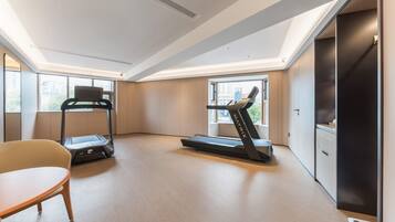 Quarto moderno com esteira, uma cadeira e vista para a cidade através de grandes janelas.