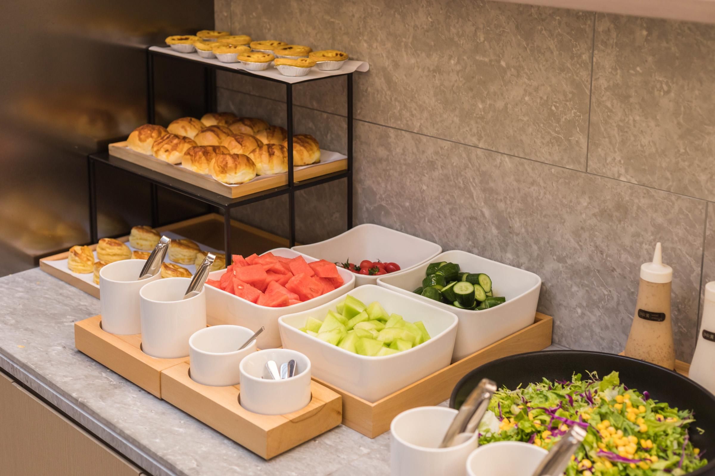 Uma mesa de buffet com diversos alimentos, incluindo pães, frutas e saladas.
